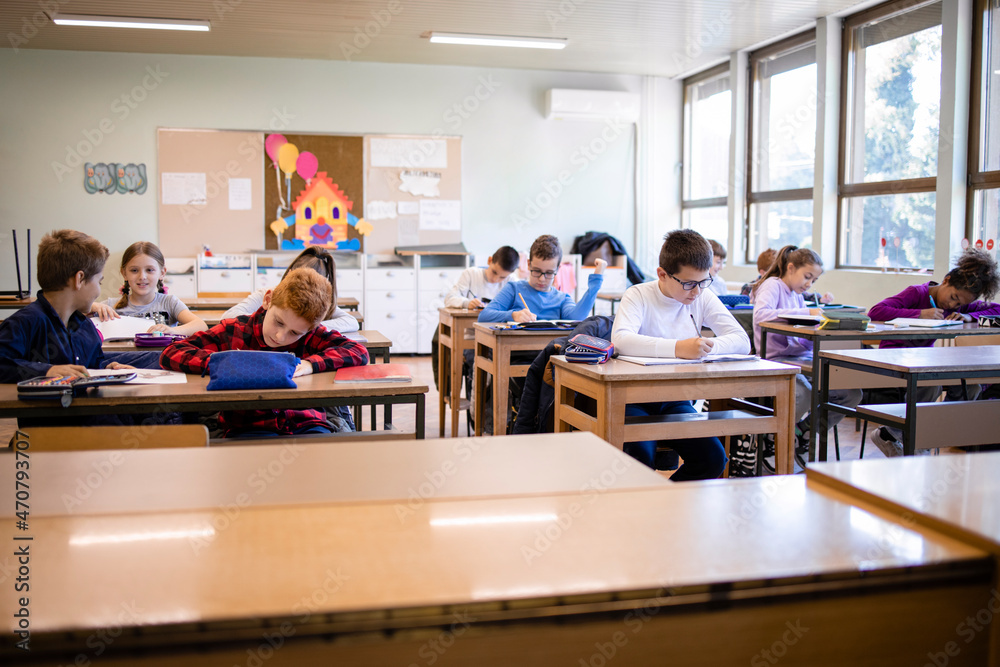 Group of concentrated school children sitting in classroom and writing ...