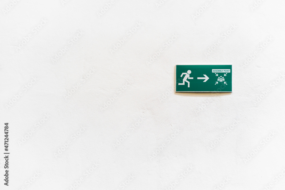 green assembly point signage on white concrete wall for background ...