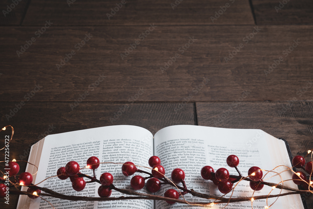 Open bible on wood background with border of red berries and Christmas ...