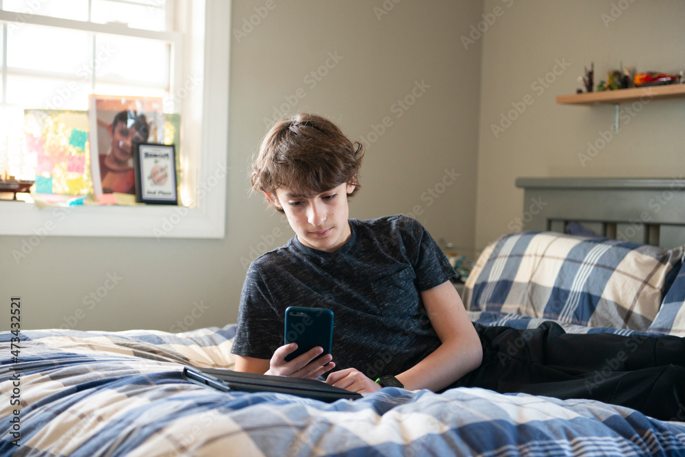 Tween boy laying on bed with phone and tablet. Stock Photo | Adobe Stock
