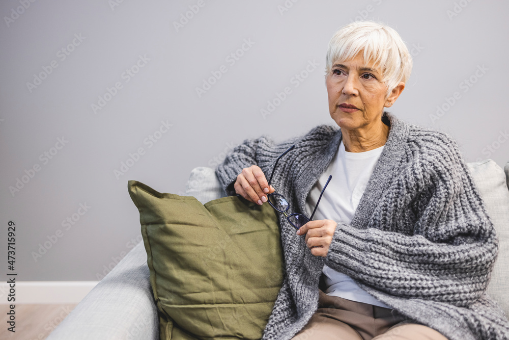 Pensive thoughtful middle aged lady looking away sit alone at home feel ...