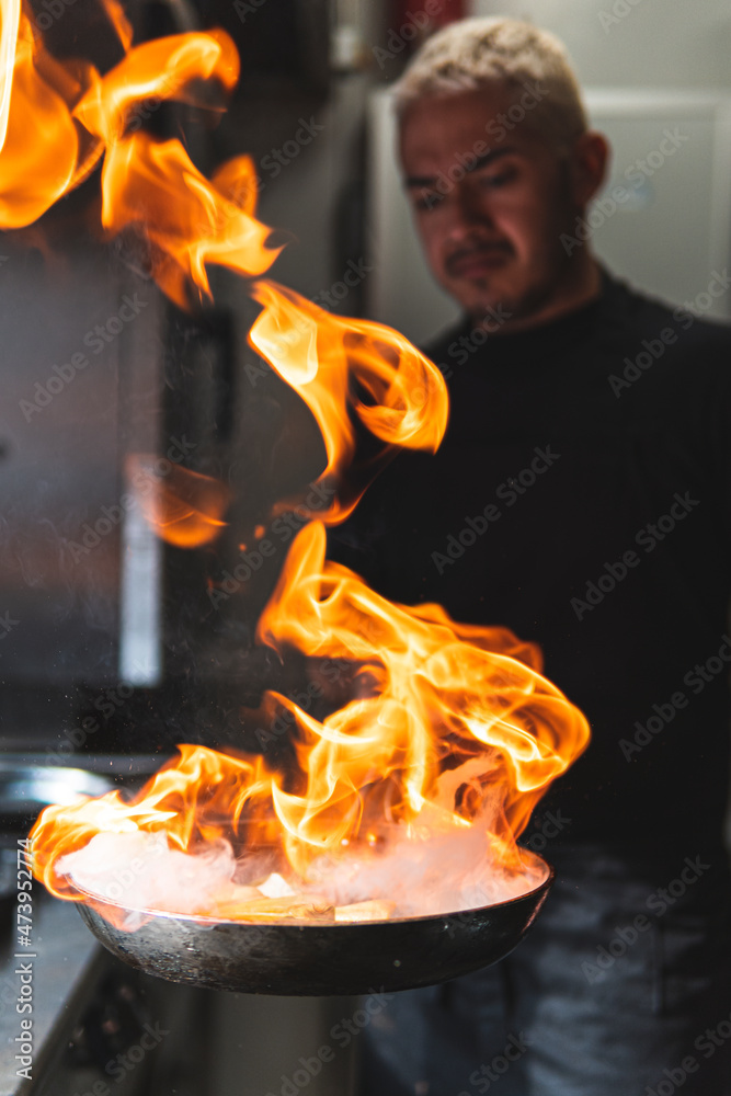 Chef holding flaming pan in kitchen Stock Photo | Adobe Stock