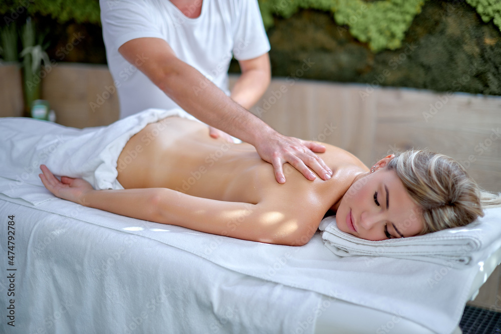 male masseur with strong hands professionally massaging scapulas and shoulders. Beautiful naked ...