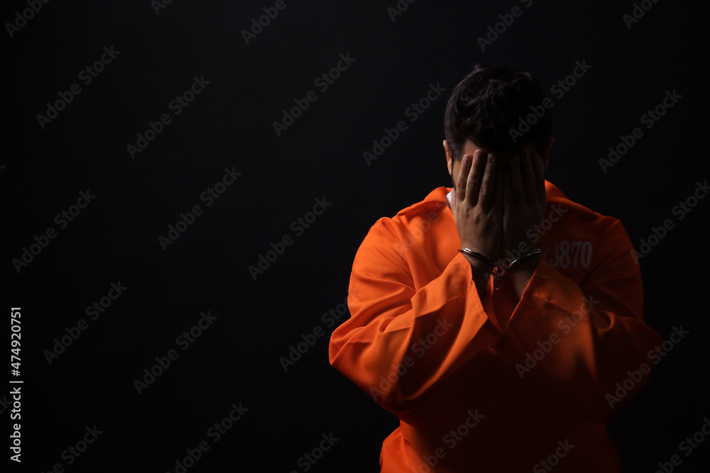 Prisoner in jumpsuit with handcuffs on black background, space for text ...