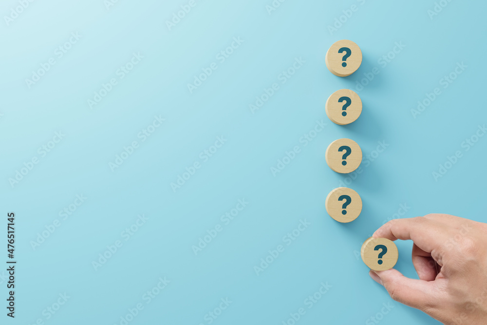 Hand holding wooden block shape with sign question mark symbol on blue ...