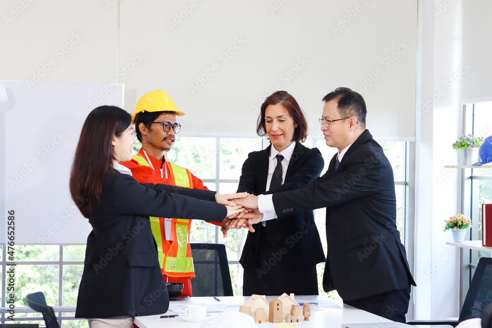 Business people and engineer putting hands together over meeting desk ...
