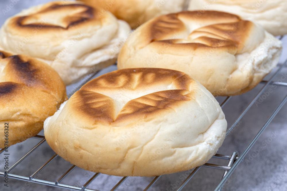 Freshly baked English muffins cooling on a metal rack. On a concrete ...
