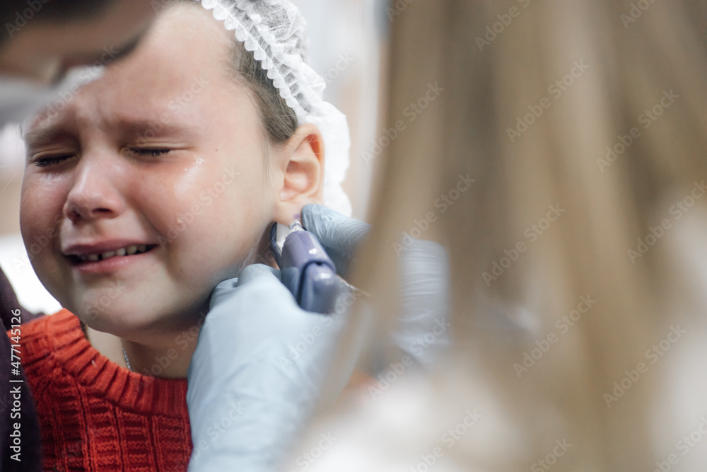 Cosmetologist wearing disposable medical gloves pierce ear with gun for ...