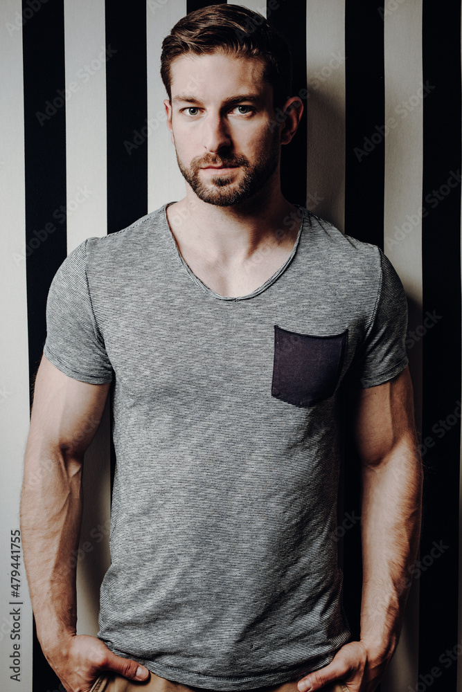 well trained male standing next to wall with hands in pockets look at ...