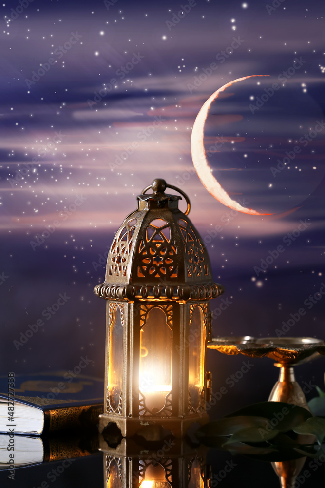 Glowing Muslim lamp and Quran on table at night. Ramadan celebration ...