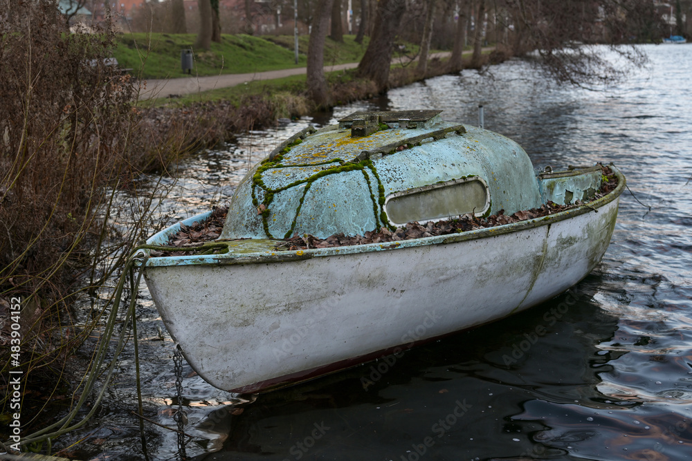 Abandoned small cabin boat made of glass fiber reinforced plastic overgrown with moss and lichen ...