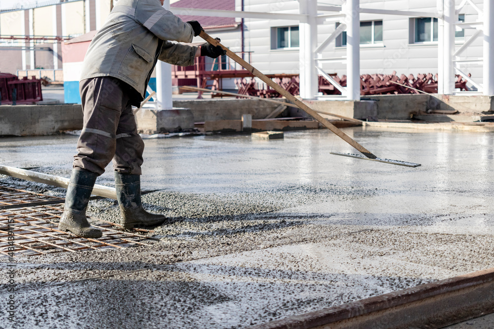 Construction worker leveling a poured concrete floor in an industrial ...