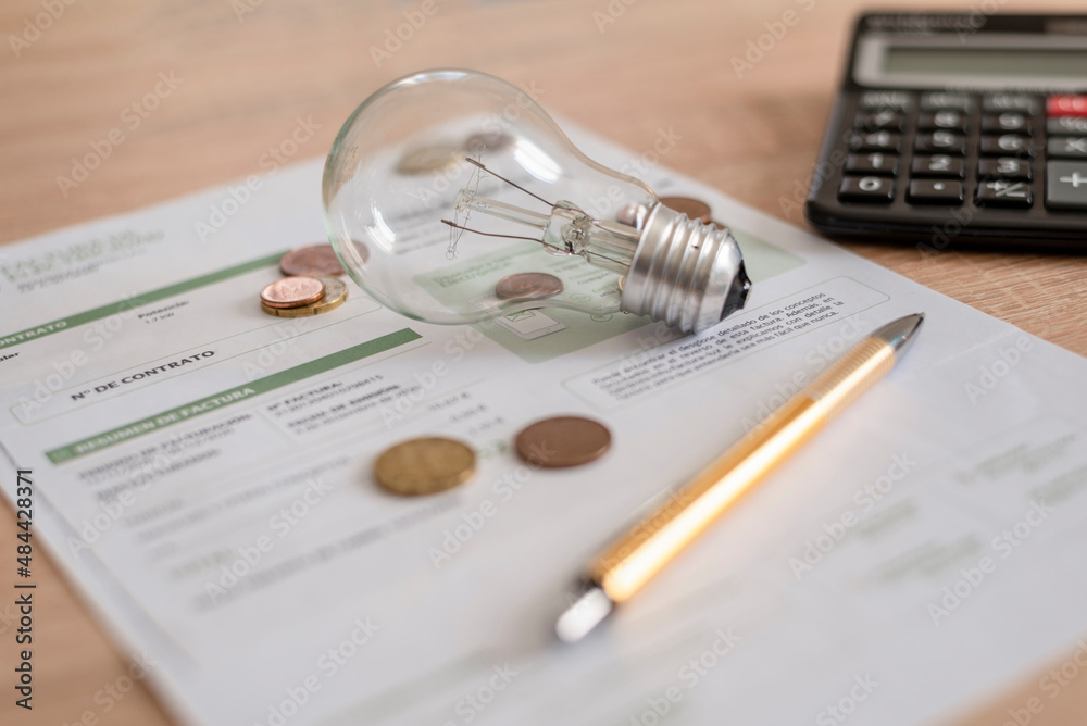 Electricity bill with light bulb, several coins, calculator and pen on ...