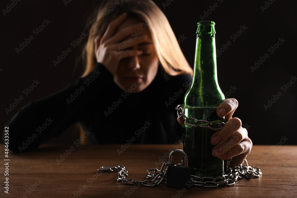 Alcohol addiction. Woman chained with bottle of beer at wooden table ...