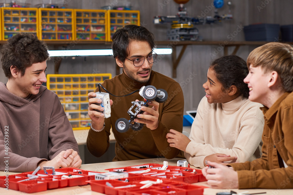 Portrait of young teacher helping diverse group of kids building robots ...