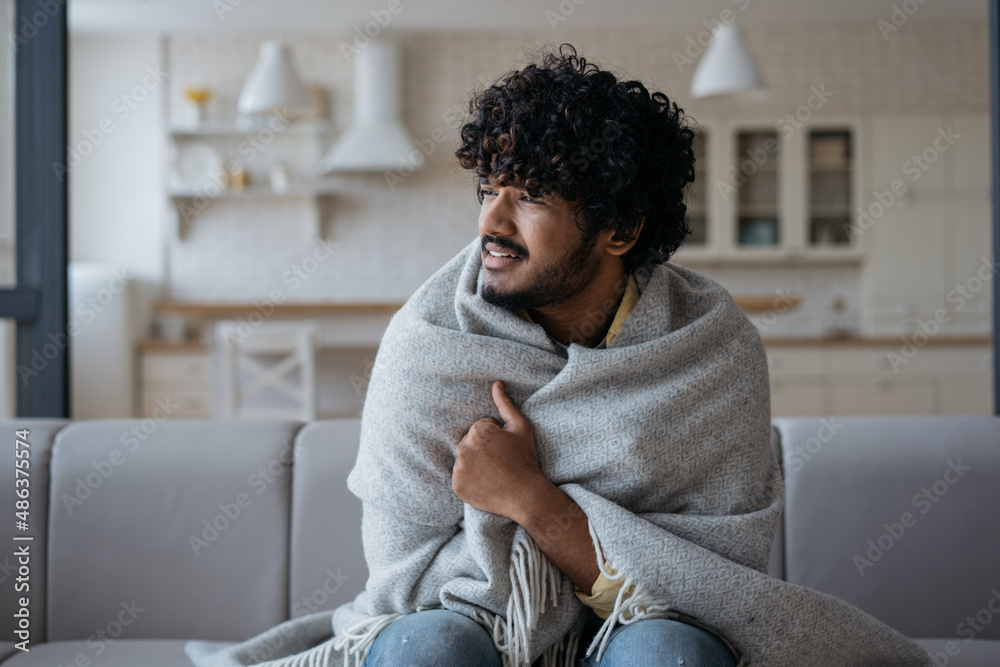 Sick unhappy Indian man covered with plaid blanket sitting in cold ...