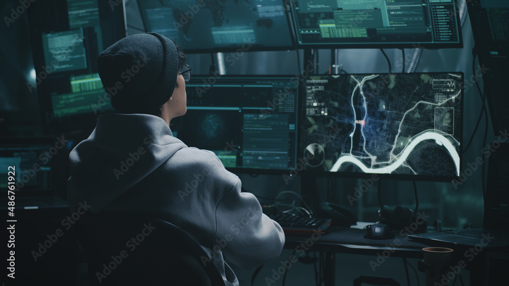 Teenage hacker with glasses watching a car on a monitor and pressing a ...