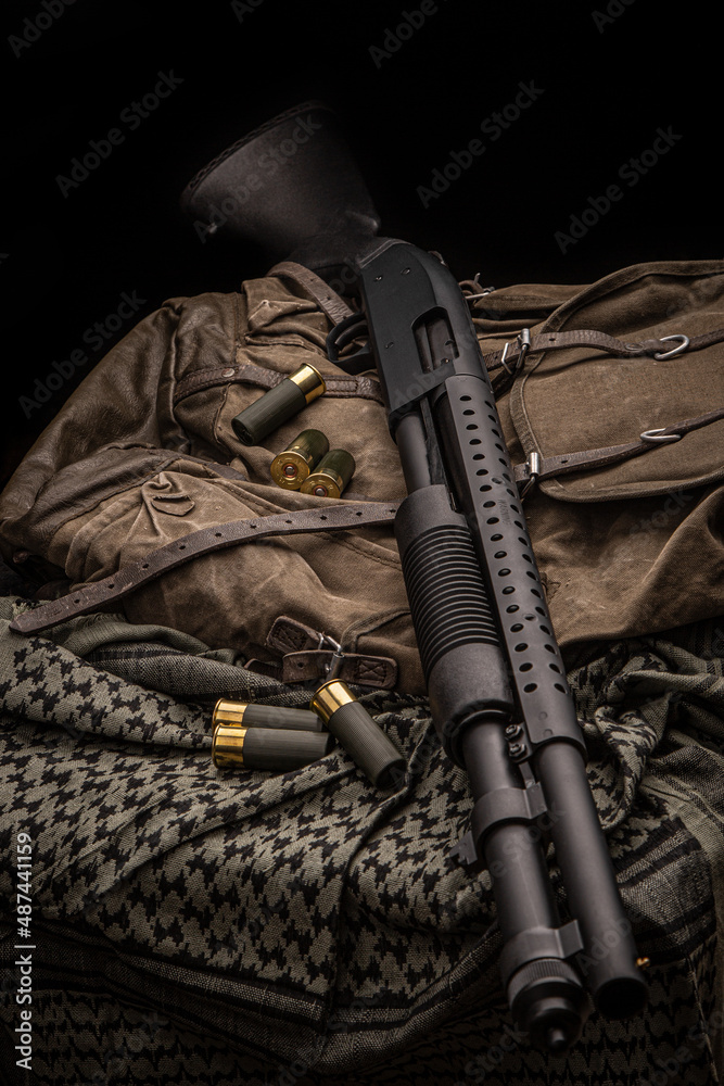 A black 12-gauge pump-action shotgun and ammo are on a canvas backpack ...