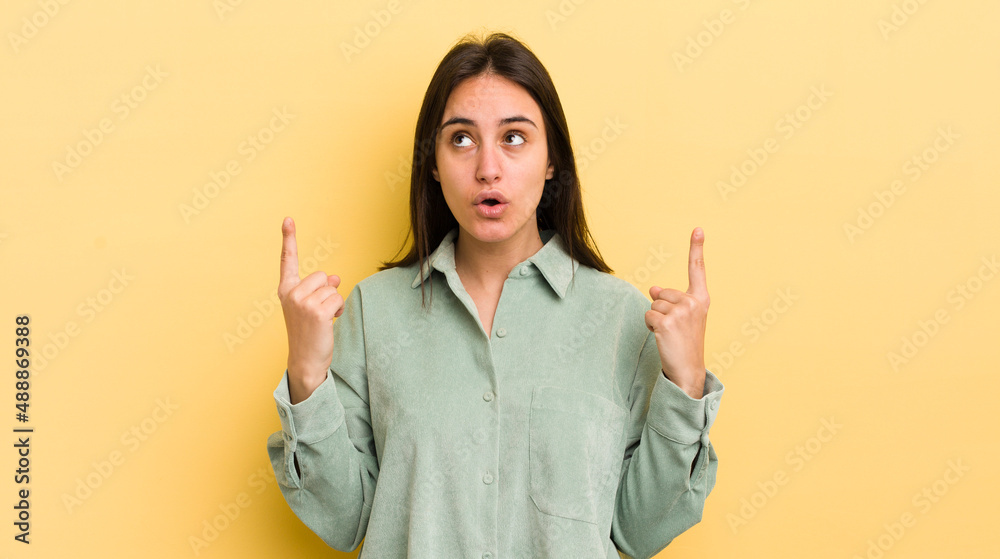 young hispanic woman feeling awed and open mouthed pointing upwards ...