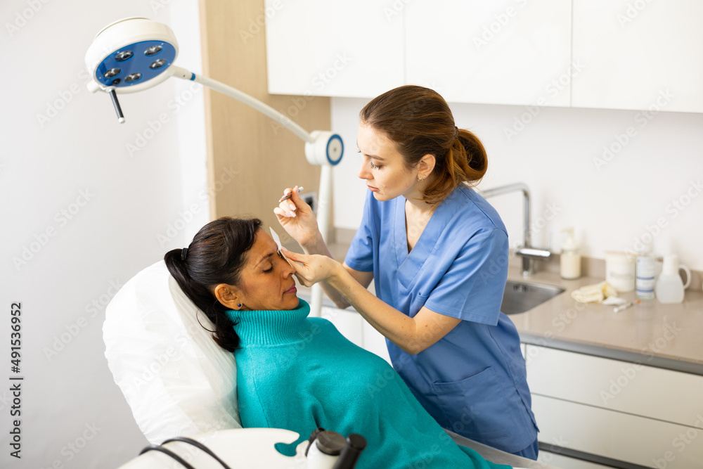 Skilled woman beautician drawing correction lines on woman face in ...