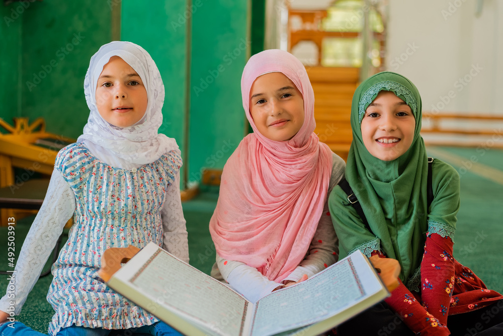 Group of a children reading a holy book Quran in the mosque. Happy Muslim family. Muslim girls ...