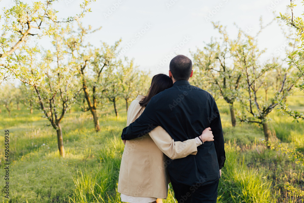 Back view of romantic couple in spring blooming garden, hugging and ...