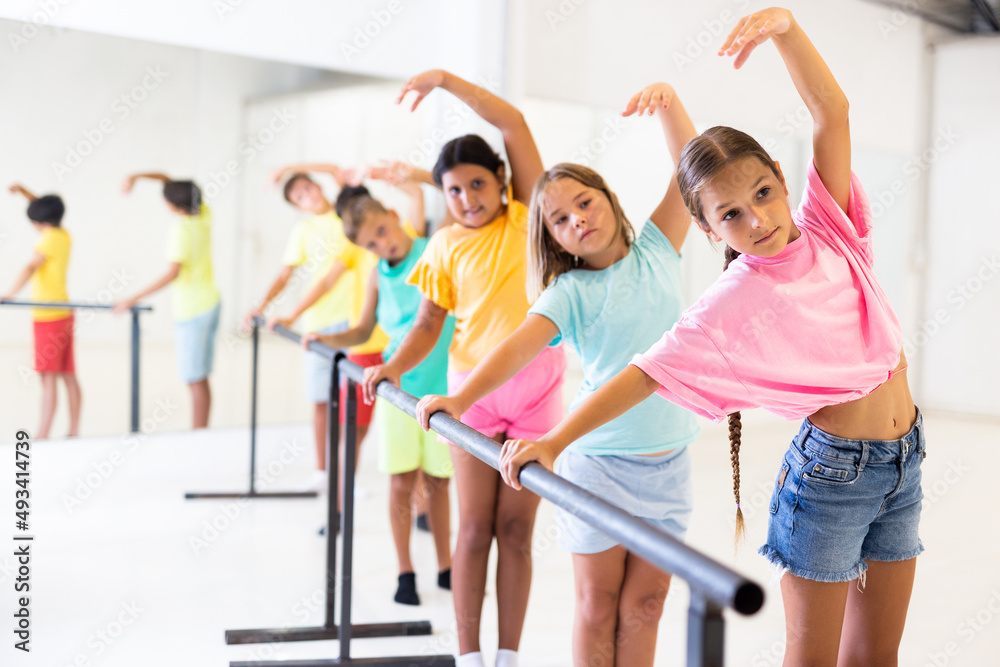 Diligent tween girl practicing classic dance moves near ballet barre ...