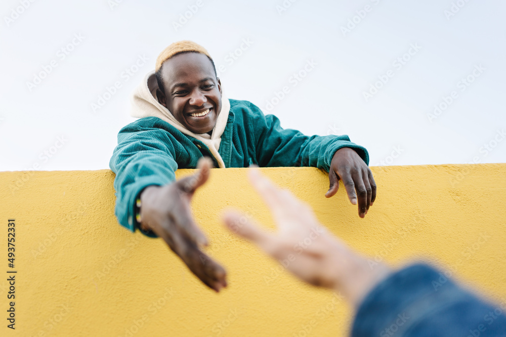 Black African Man helping caucasian friend offering hand to climb wall ...