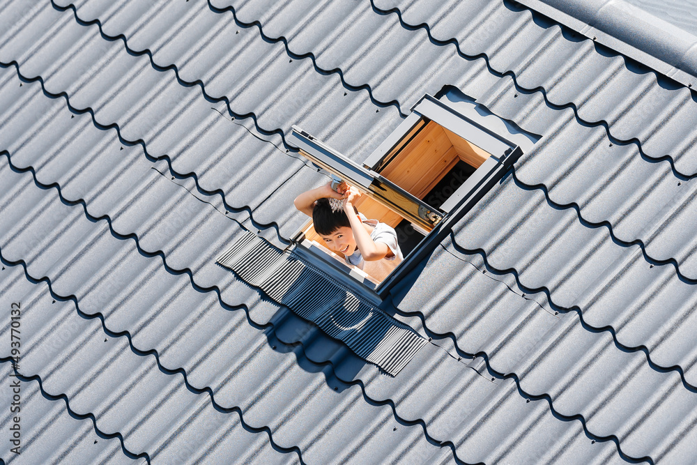 Little happy boy opens roof window on sunny morning. Roof is covered ...