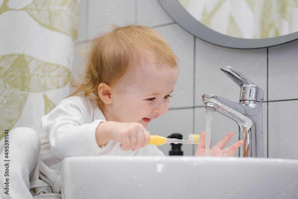 A toddler sitting on the washbasin cabinet and brushing teeth, washing ...