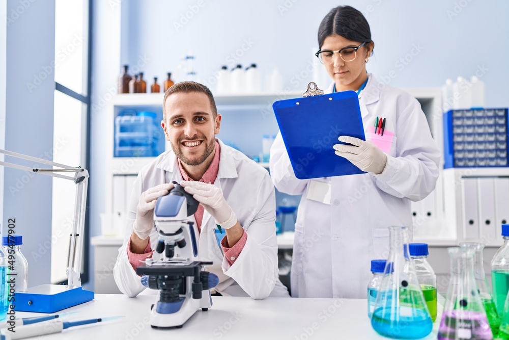 Man and woman wearing scientists uniform using microscope at laboratory ...
