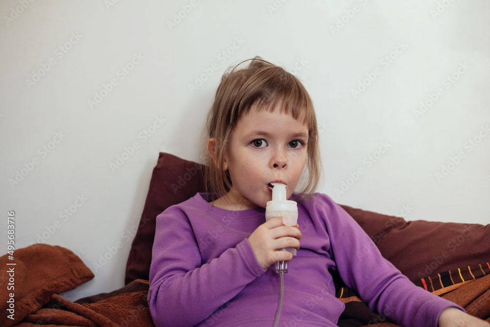 Sick child lies in bed and makes inhalation using a nebulizer ...