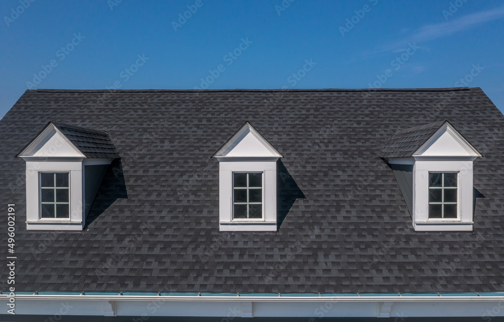 Closeup view of three white dormer windows on a classic roof with blue ...