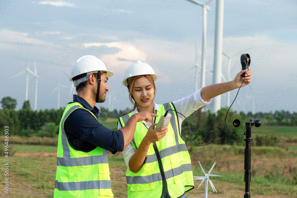Two young engineers use an anemometer to measure wind speed ...
