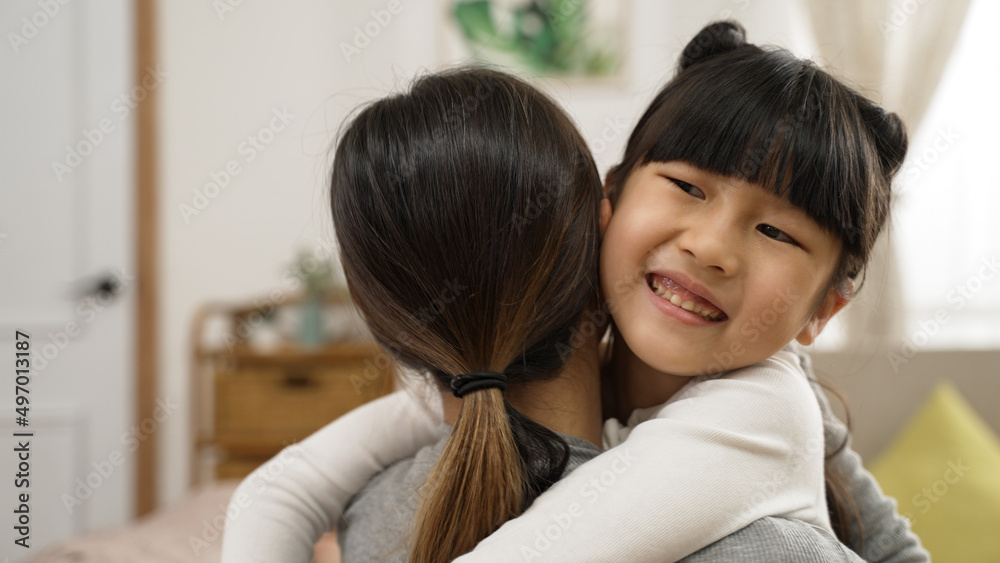 sweet asian little girl putting arms around her mom in the living room ...