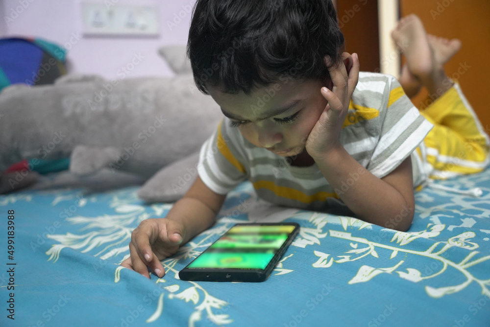 a toddler baby boy engaged in watching and exploring mobile phone ...