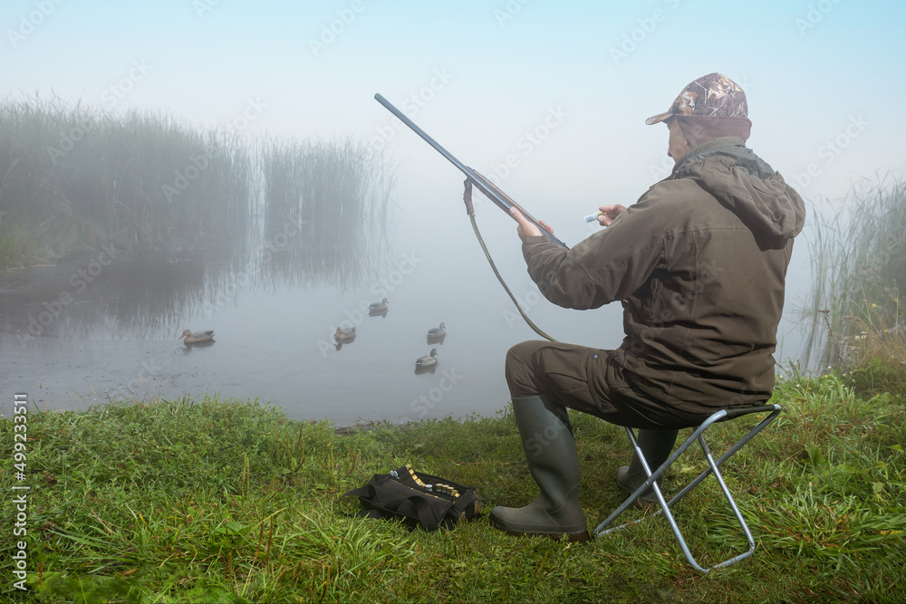 Man hunter charges the shotgun near rive bank at sunrise. Duck Hunting ...