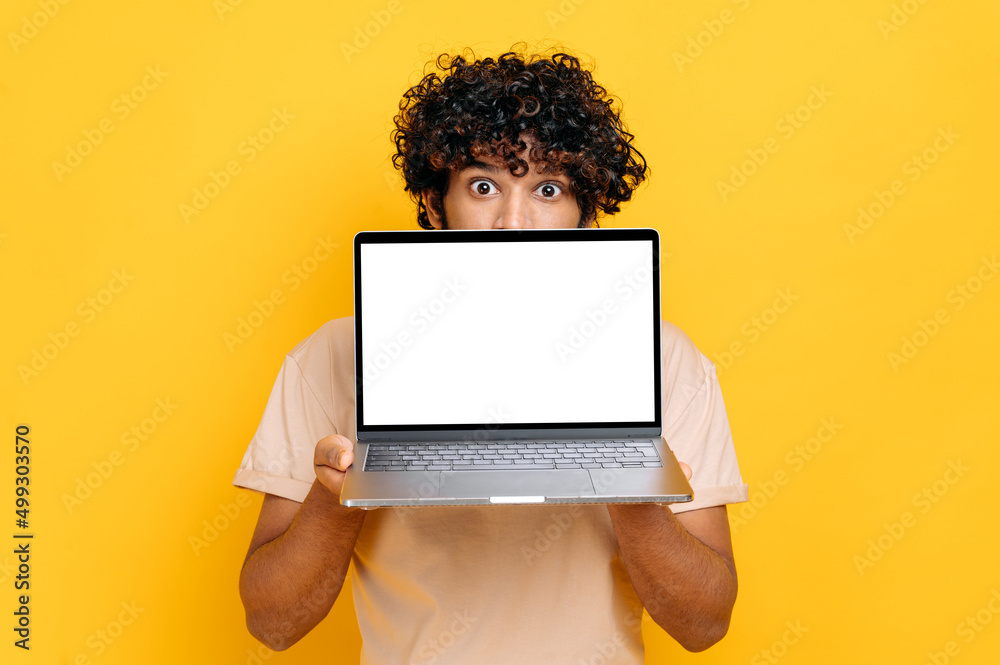 Amazed excited indian or arabian guy, peeking out from behind laptop ...