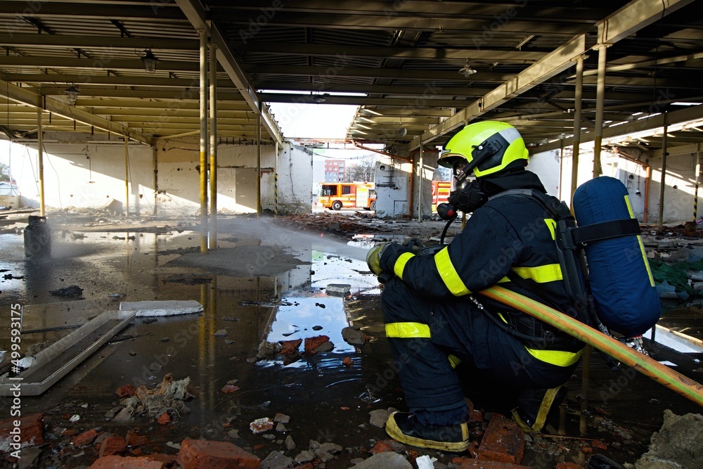 Firefighter with breathing apparatus uses a stream of water to cool a ...