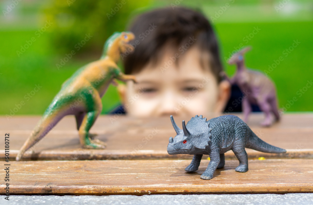 cute kid is playing with dinosaurs toys on park bench, spring, green ...
