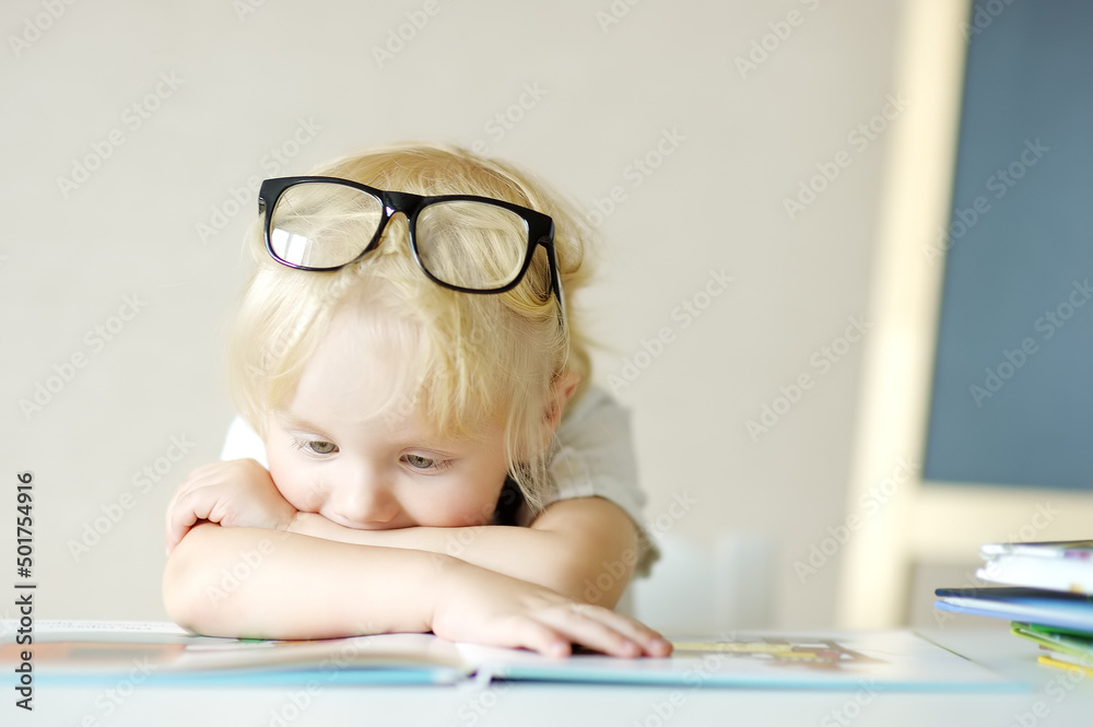 Little child wearing glasses is having fun with a book. Cute boy is ...
