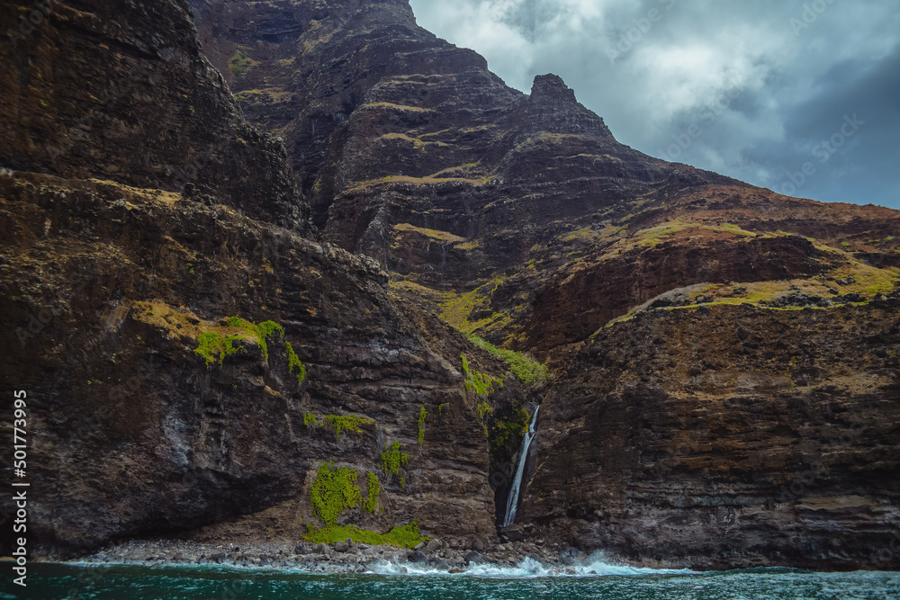 Small waterfall falls through the red rocks of the Napali Coast in ...