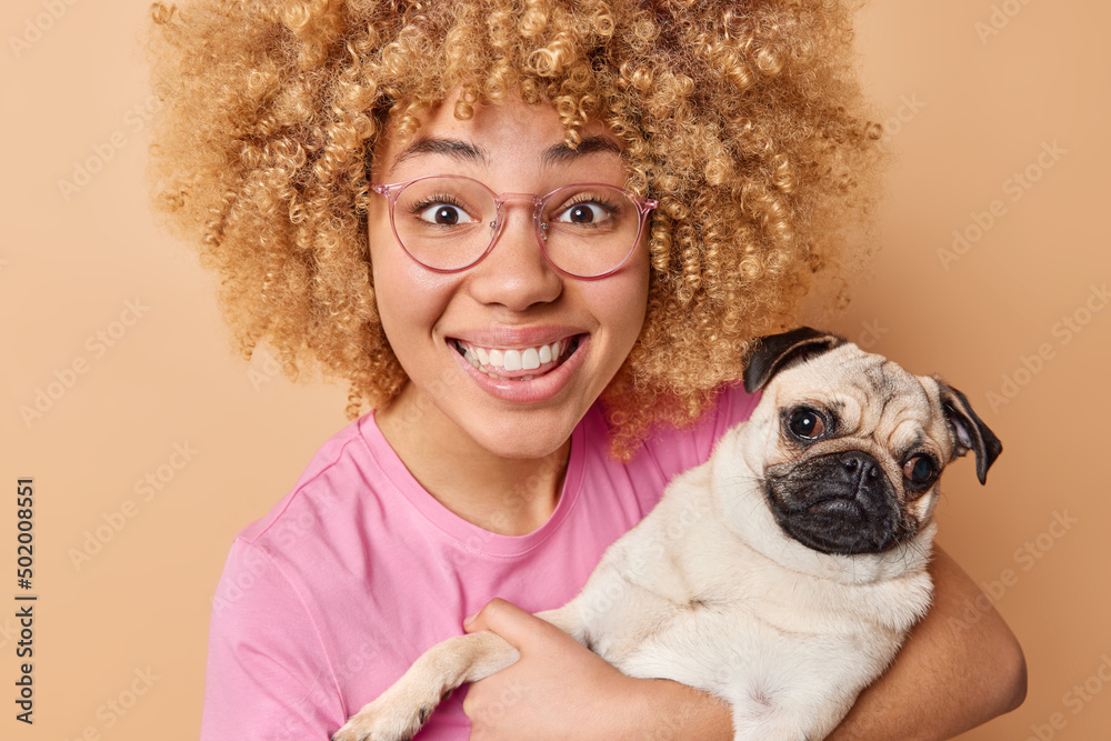 Portrait of happy woman with blonde curly hair embraces pug dog with ...