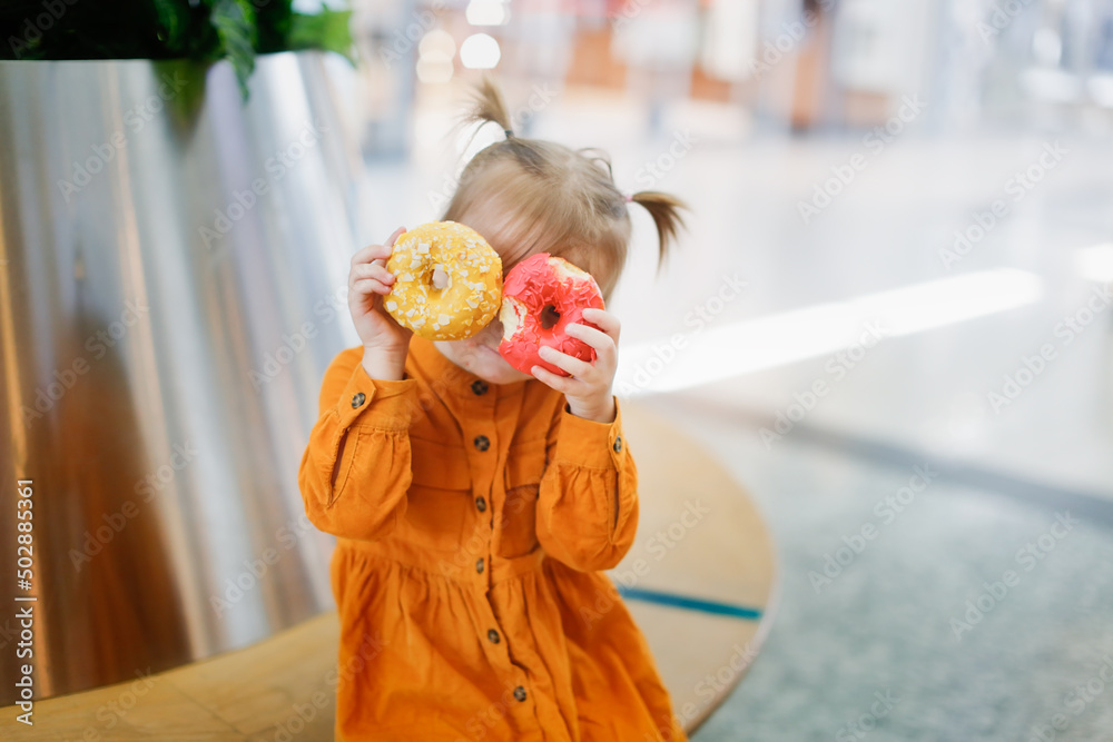 Toddler girl eats donut in supermarket on bench, snack with pastries ...