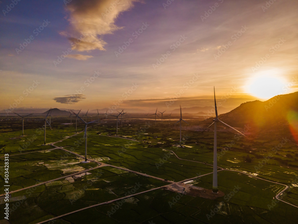 Wind turbines farm in a big green field at beautiful sunset generating ...