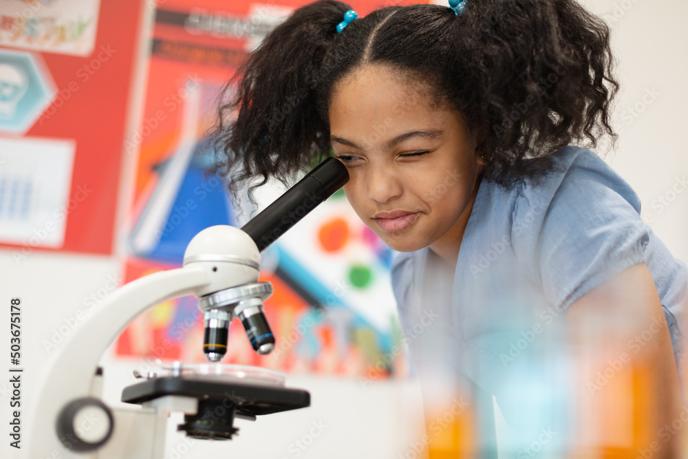 Biracial elementary schoolgirl looking through microscope during ...