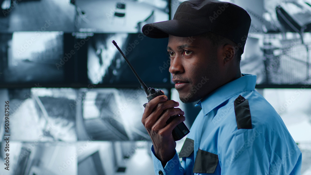 Side view of African-American security guard talk on radio in control ...