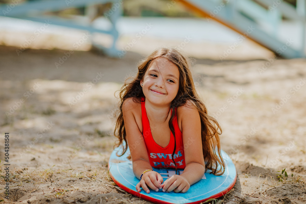 Pretty young girl in red bikini posing with blue surfboard on the beach against blue lifeguard ...