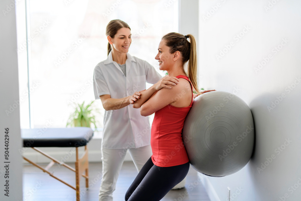 Physiotherapist helping woman do wall squats with fit ball. Young ...
