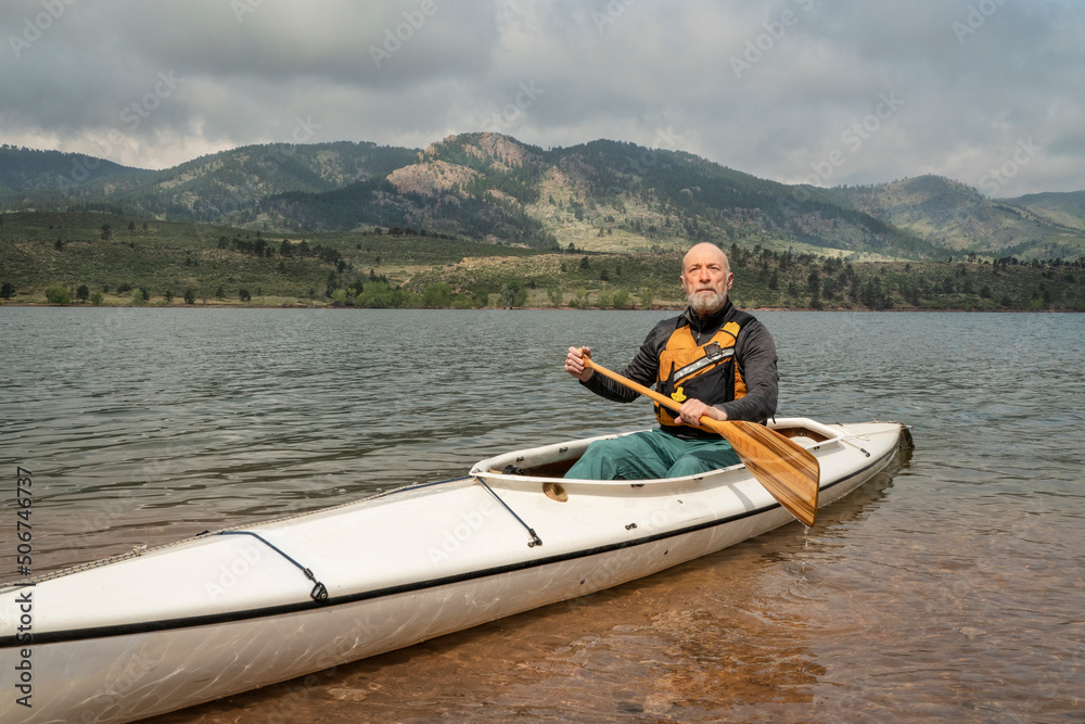 senior male wearing life jacket is paddling a decked expedition canoe ...